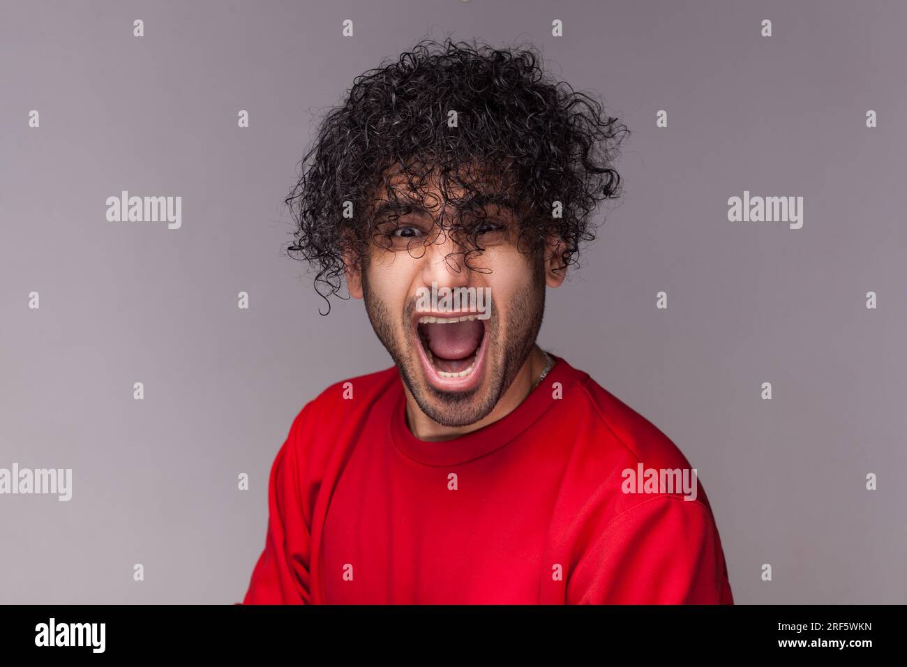 Portrait of funny angry crazy handsome young adult bearded man with curly hair, standing looking ...