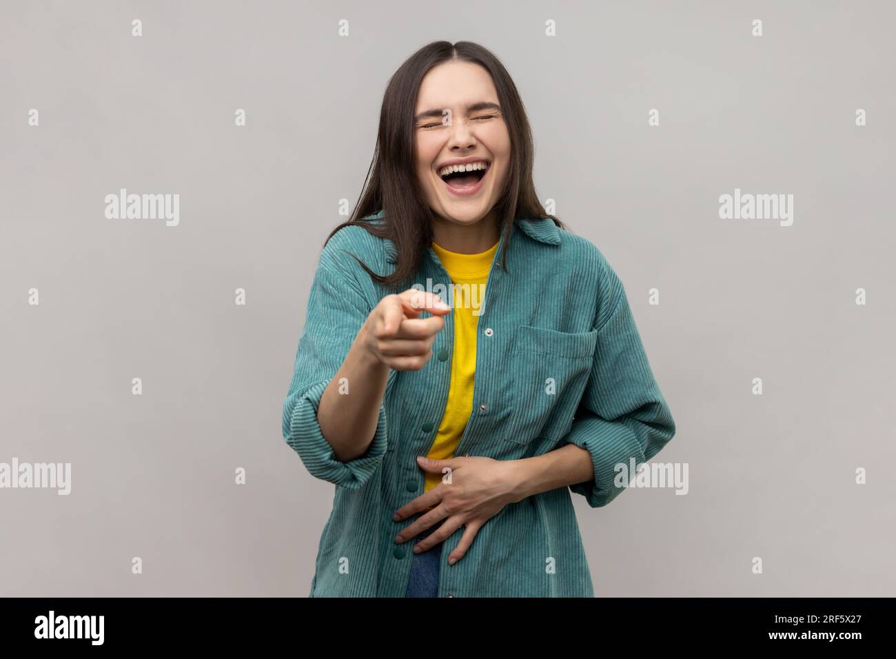 Joyful woman laughing, holding stomach, pointing to camera, taunting ...