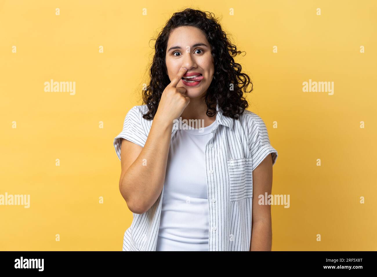 Portrait of childish woman with dark wavy hair standing, picking nose ...