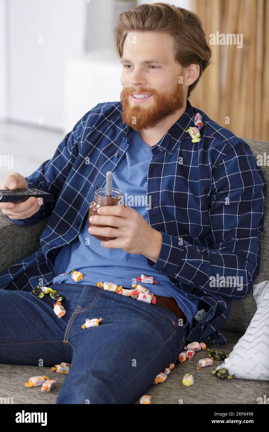 man eating chocolate holding a remote control on a couch Stock Photo ...