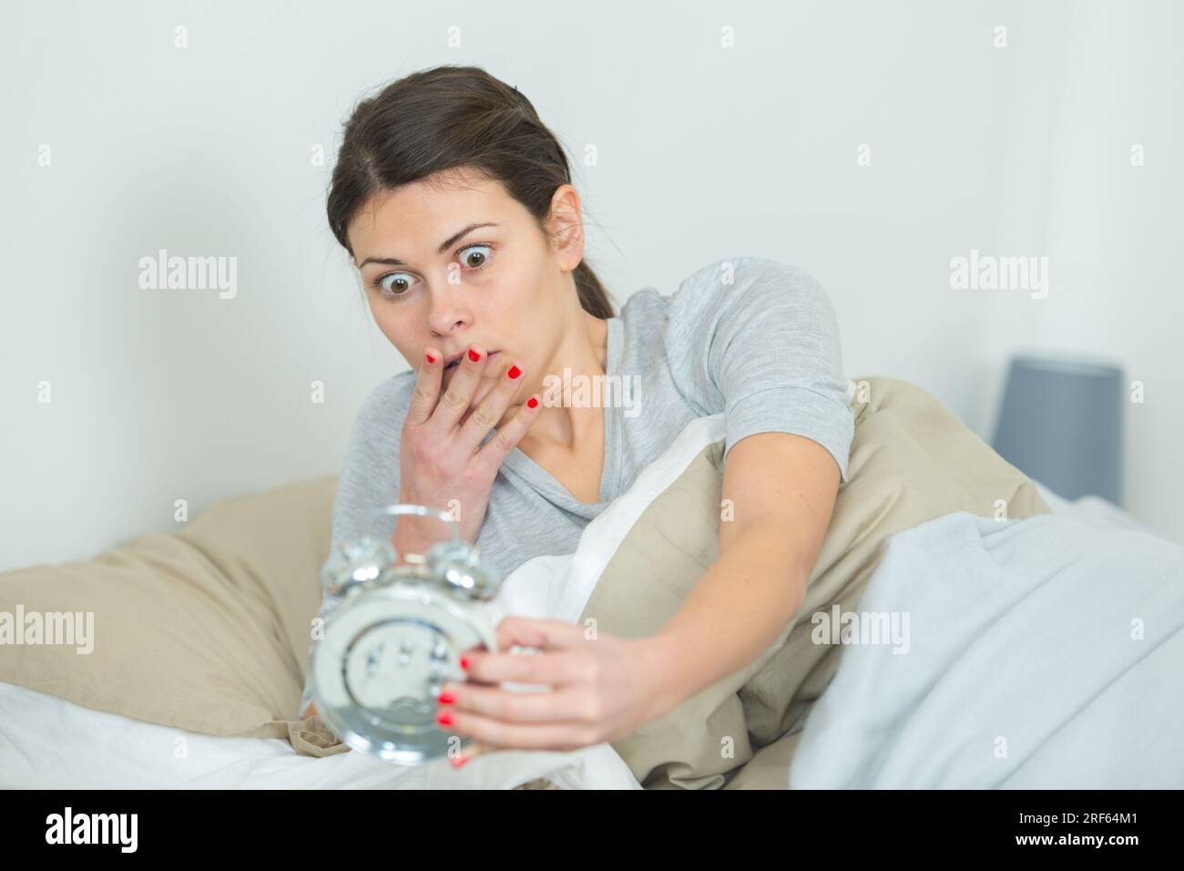 surprised woman looking at alarm clock Stock Photo - Alamy