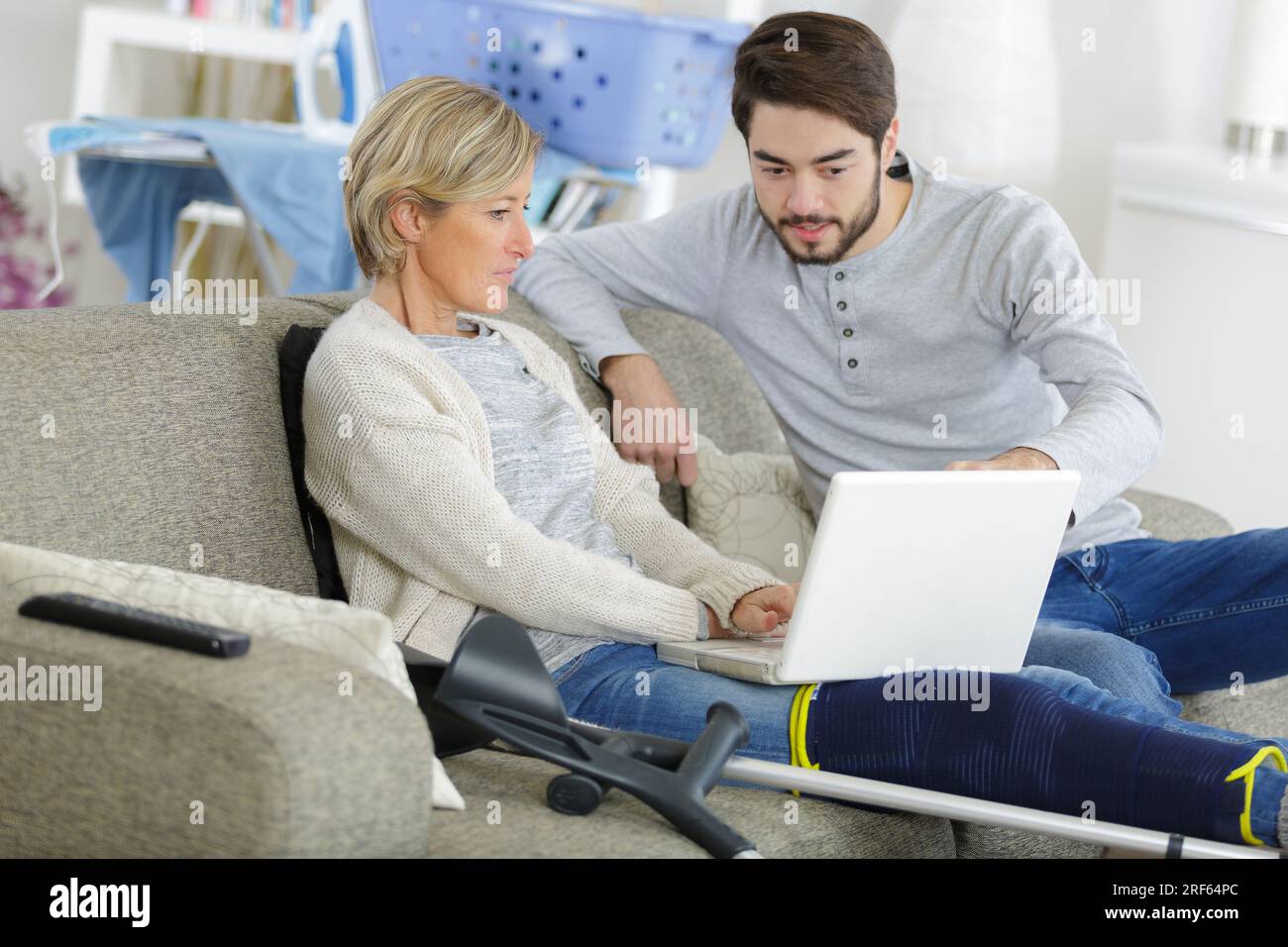 young man helping woman with leg injury to use laptop Stock Photo - Alamy