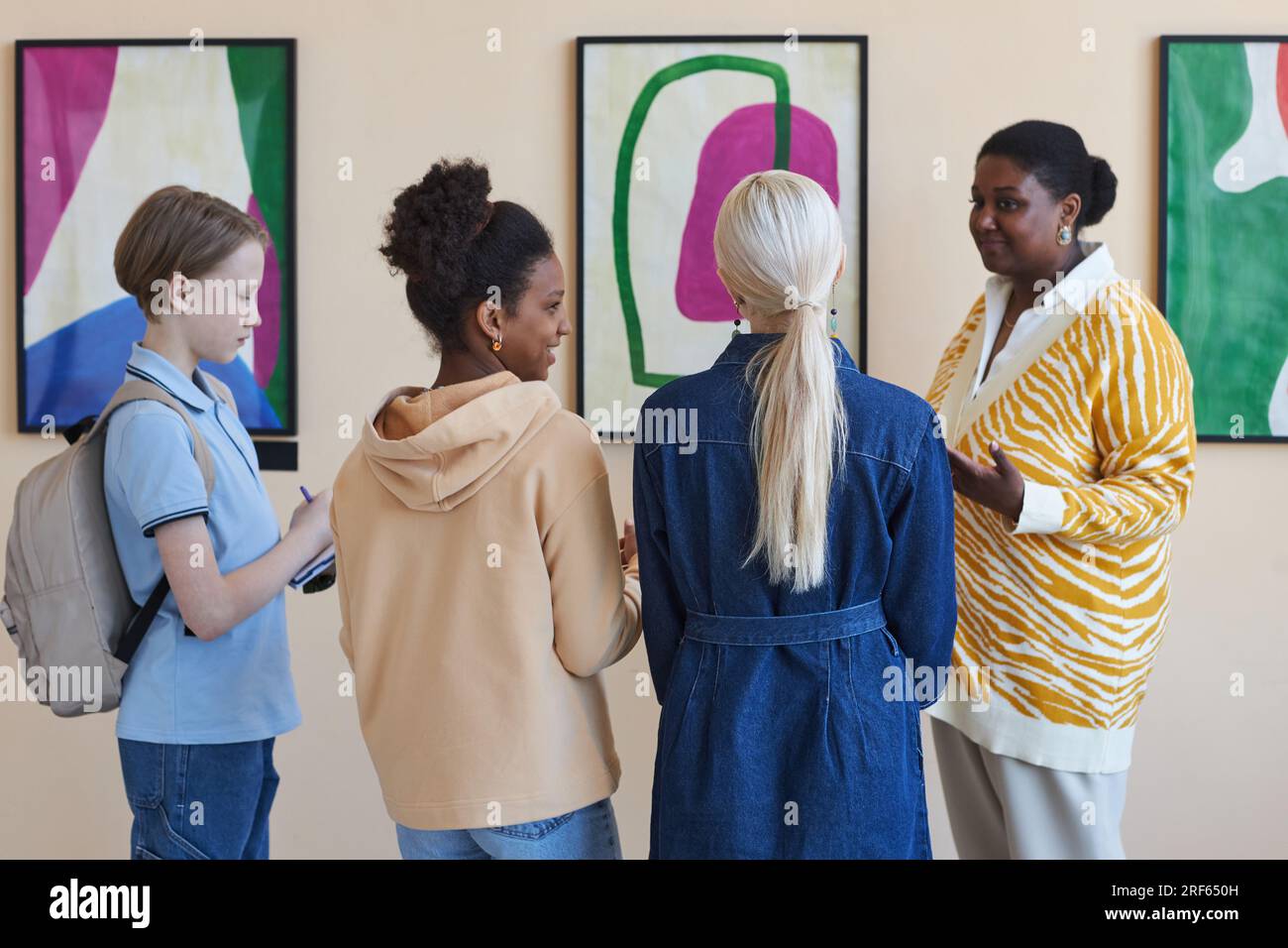 Diverse group of teenage schoolchildren listening to female tour guide ...