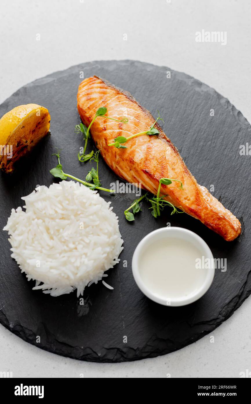 Grilled salmon steak and white rice with sauce on a stone plate on ...