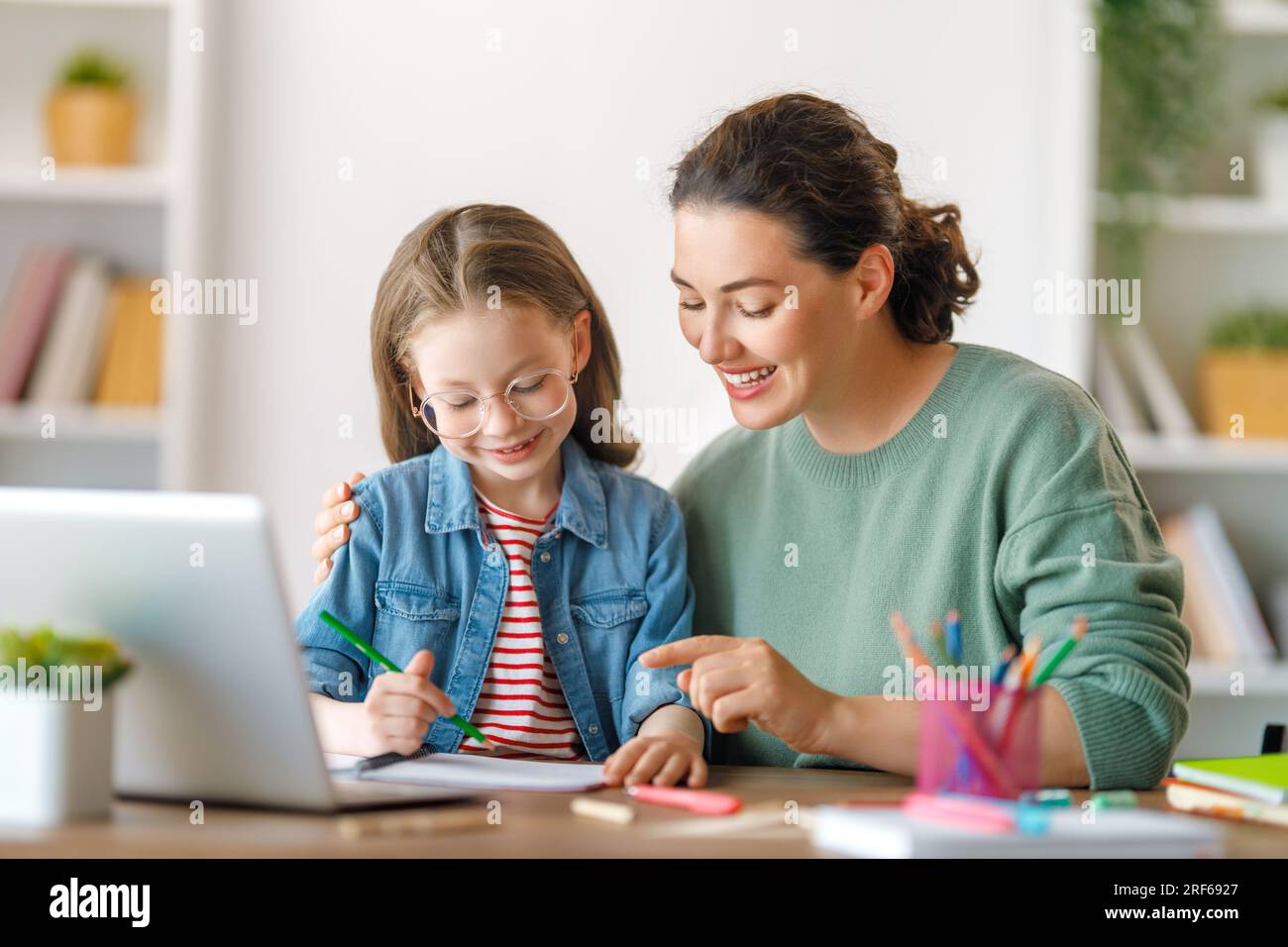 Happy child and adult are sitting at desk. Girl doing homework or ...