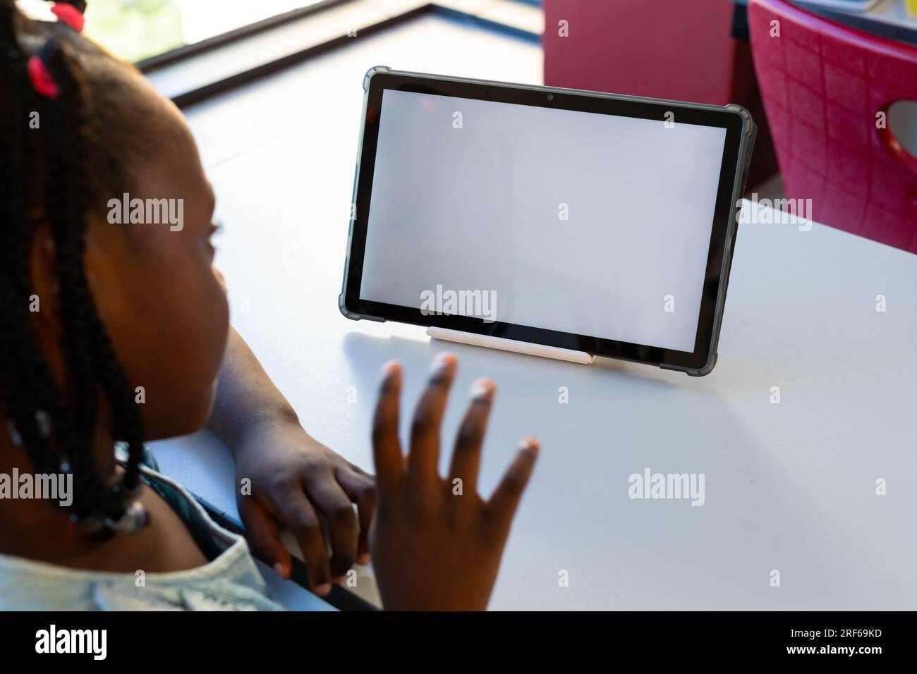 Focused african american schoolgirl using tablet with copy space at ...