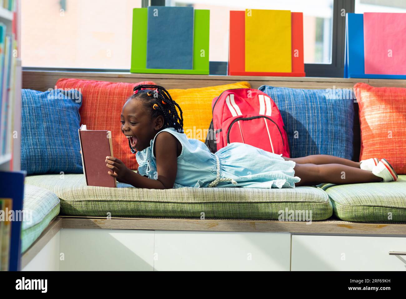 Happy african american schoolgirl reading book in colourful room at ...