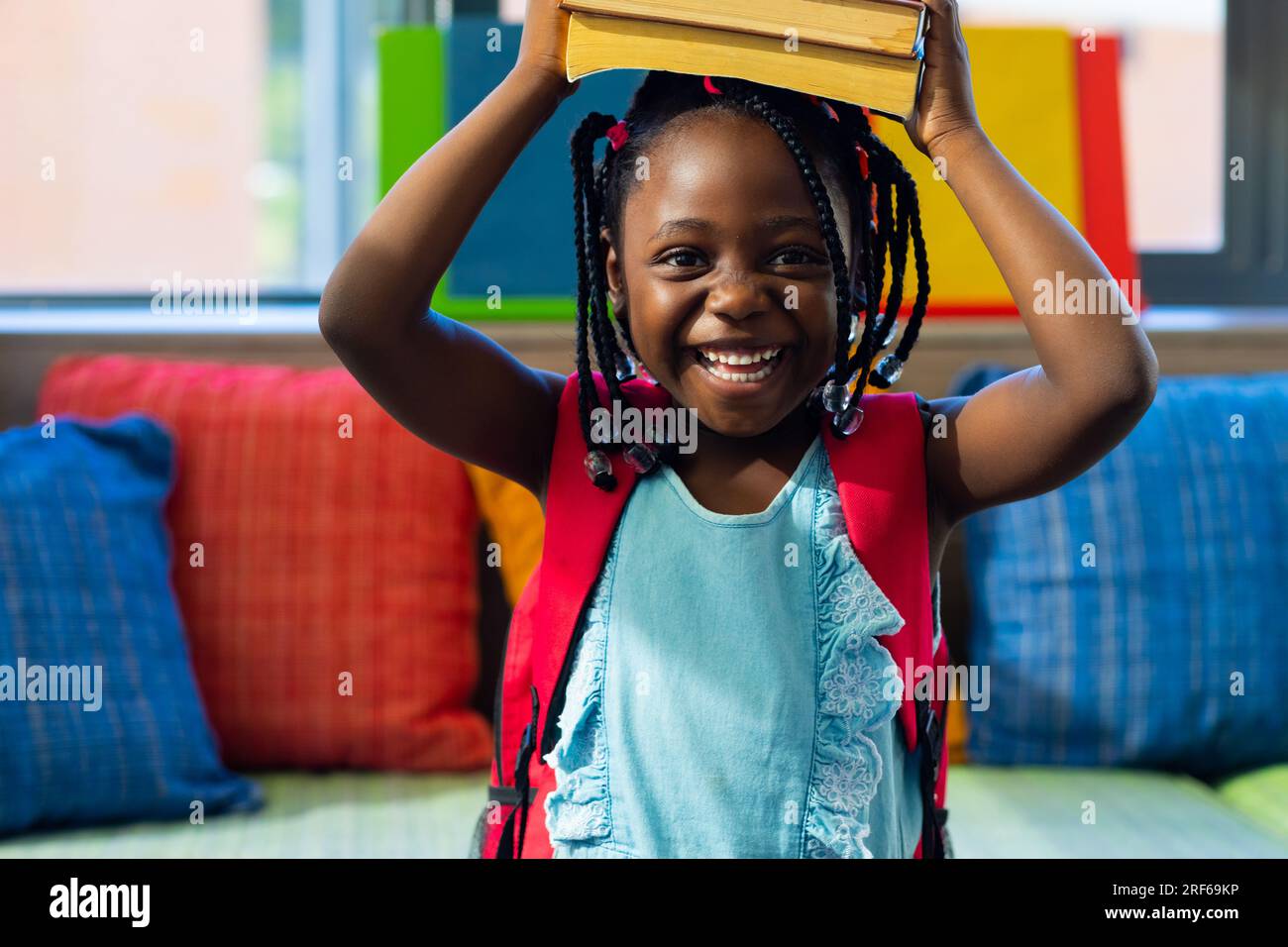 Portrait Of Happy African American Schoolgirl Holding Books Above Her