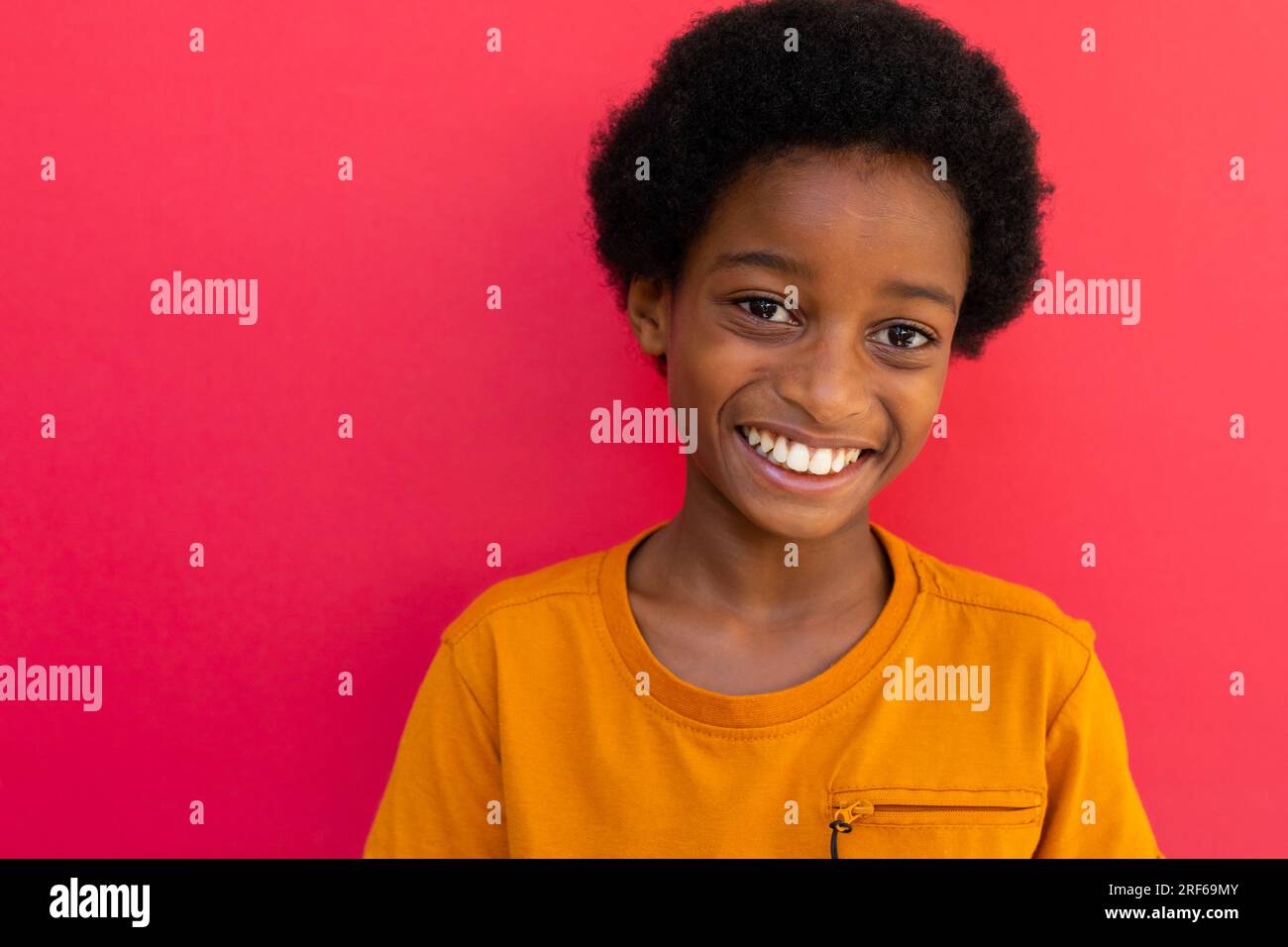 Portrait of happy biracial schoolboy wearing yellow tshirt over pink ...
