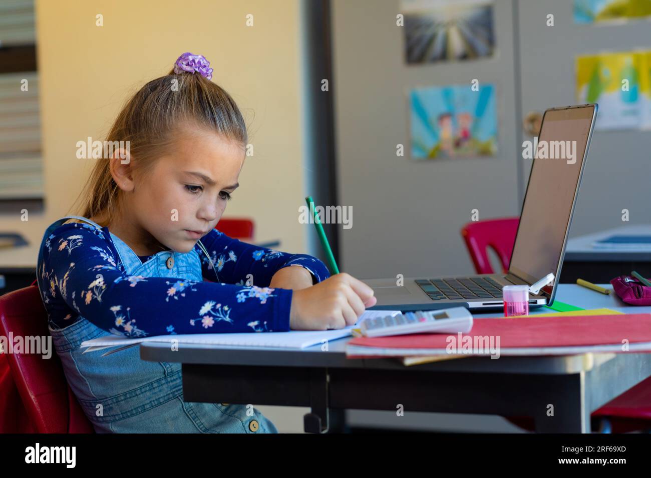 Focused caucasian schoolgirl taking notes and learning during laptop ...