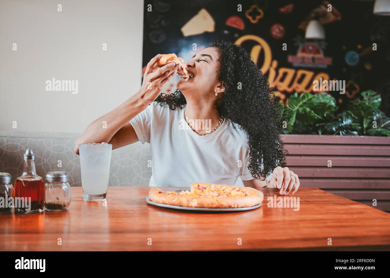 Lifestyle of afro-haired woman enjoying a pizza in a restaurant. Happy ...