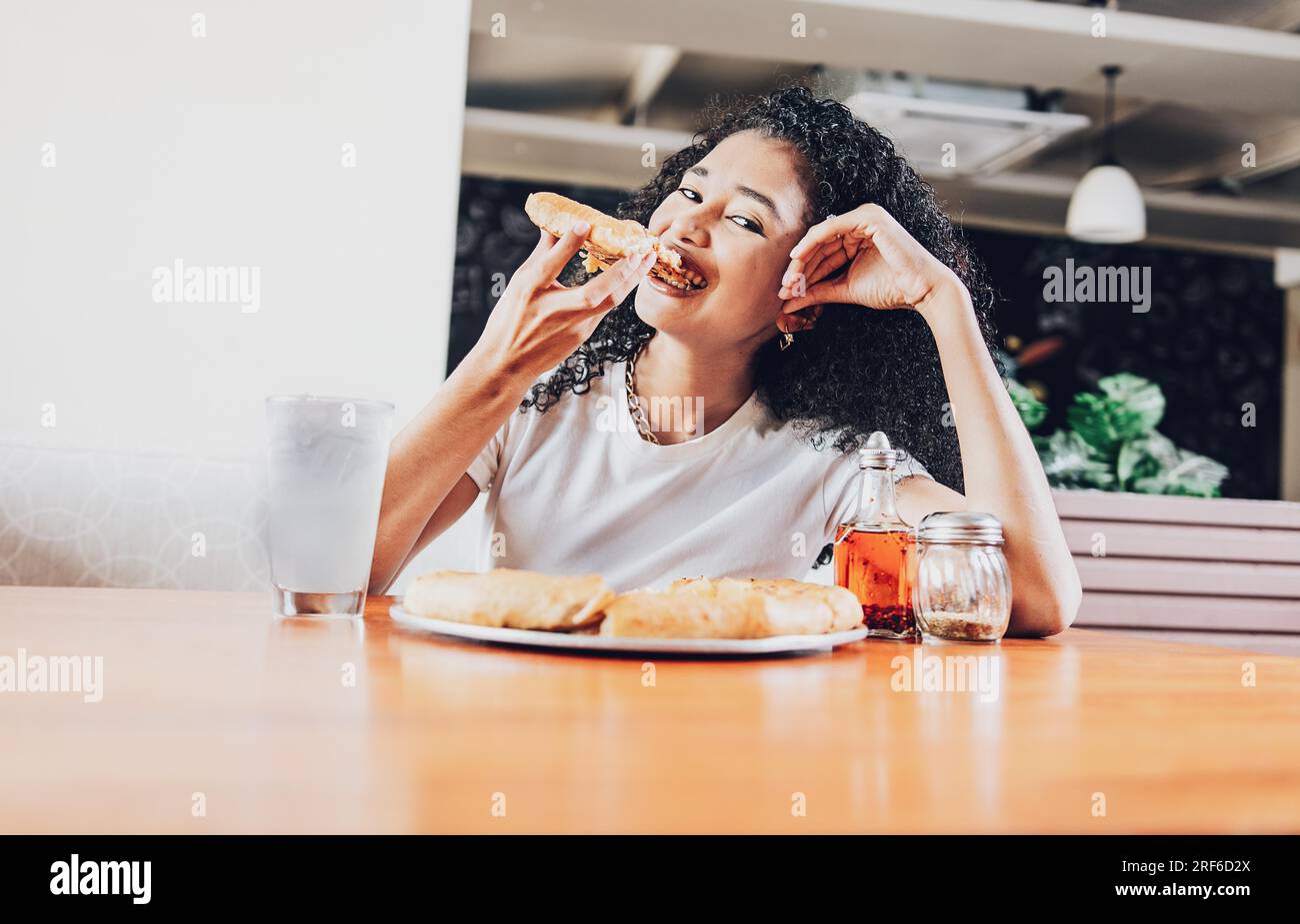 Smiling afro-haired woman enjoying a pizza in a restaurant. Happy afro ...