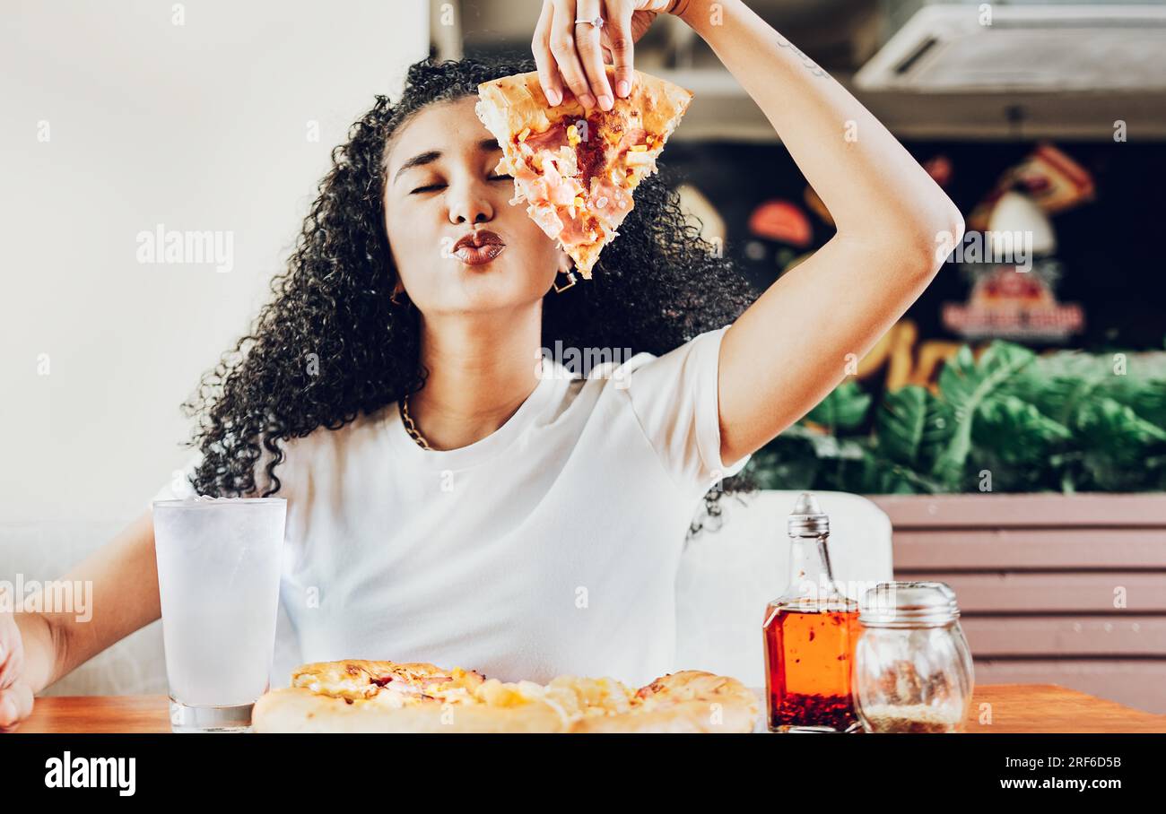 Girl in a restaurant showing slice of pizza giving a kiss to the camera ...