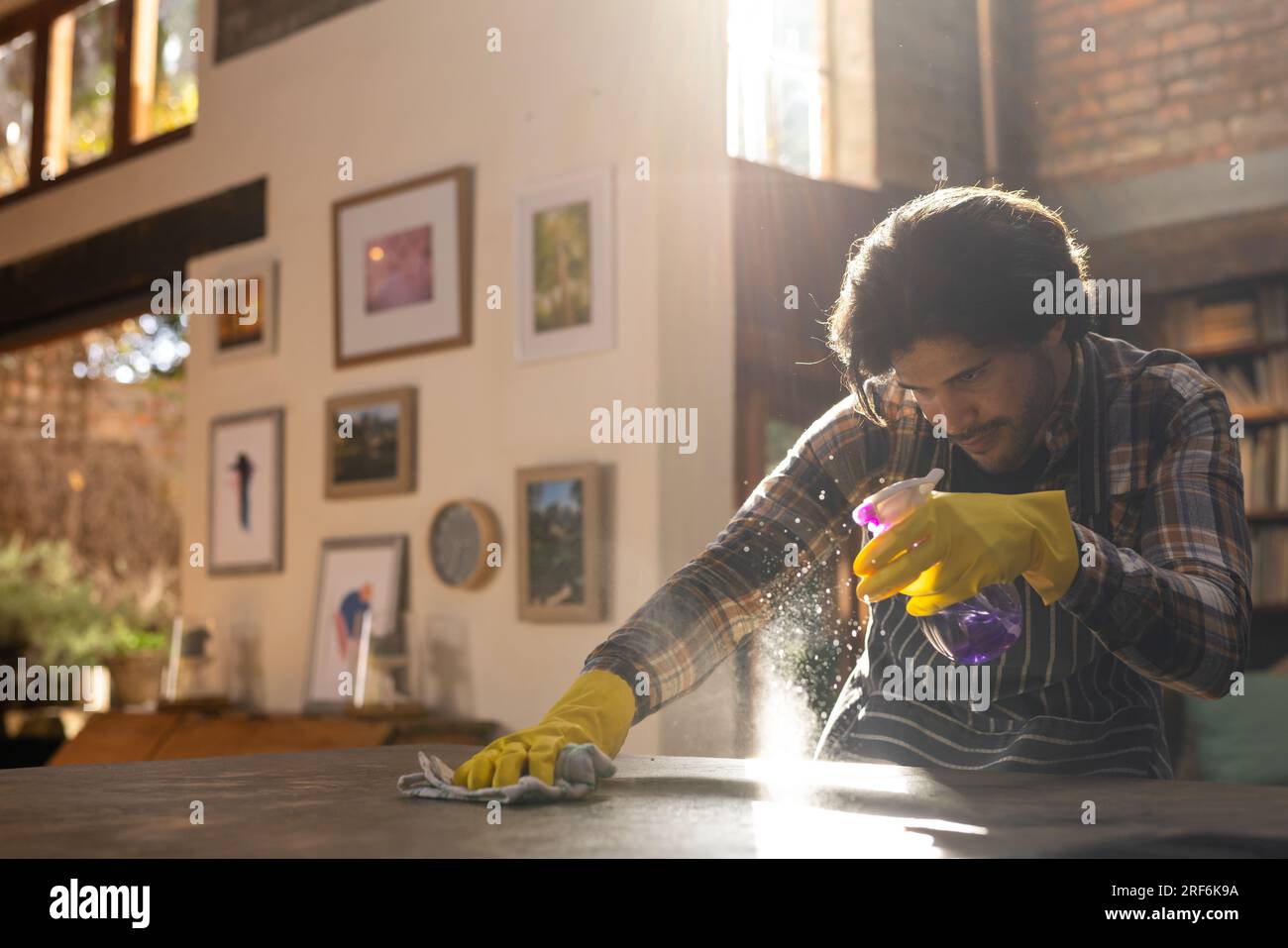 Indian man wearing yellow gloves and cleaning worktop in kitchen, copy ...