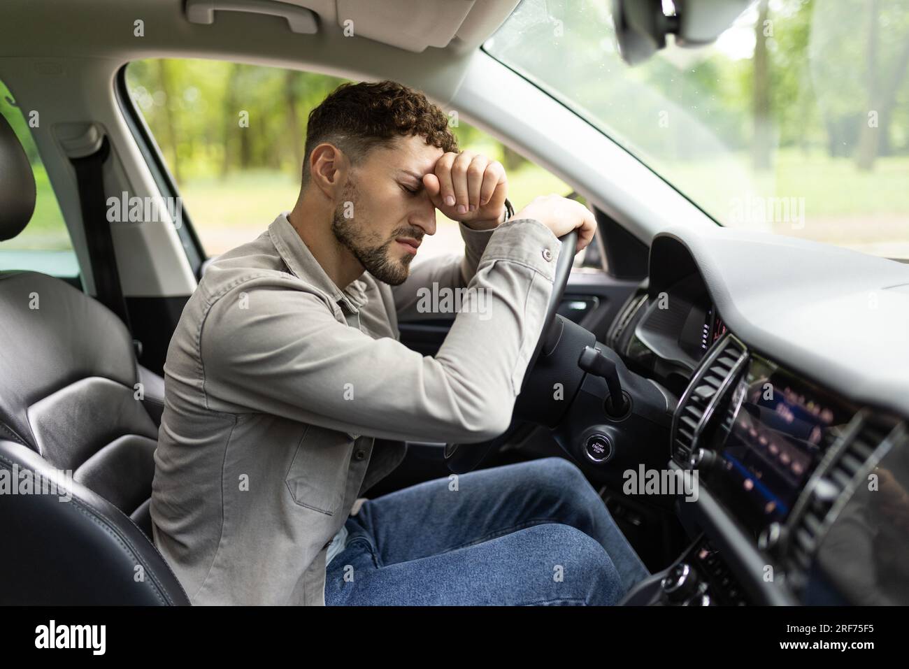 Tired man driver in suit rubbing his eyes behind steering wheel of car ...
