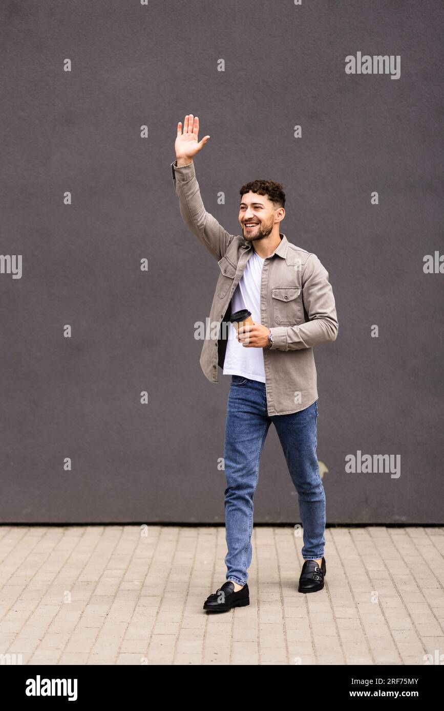 Chherful and happy young man walks on street. He waves with hand. Guy ...