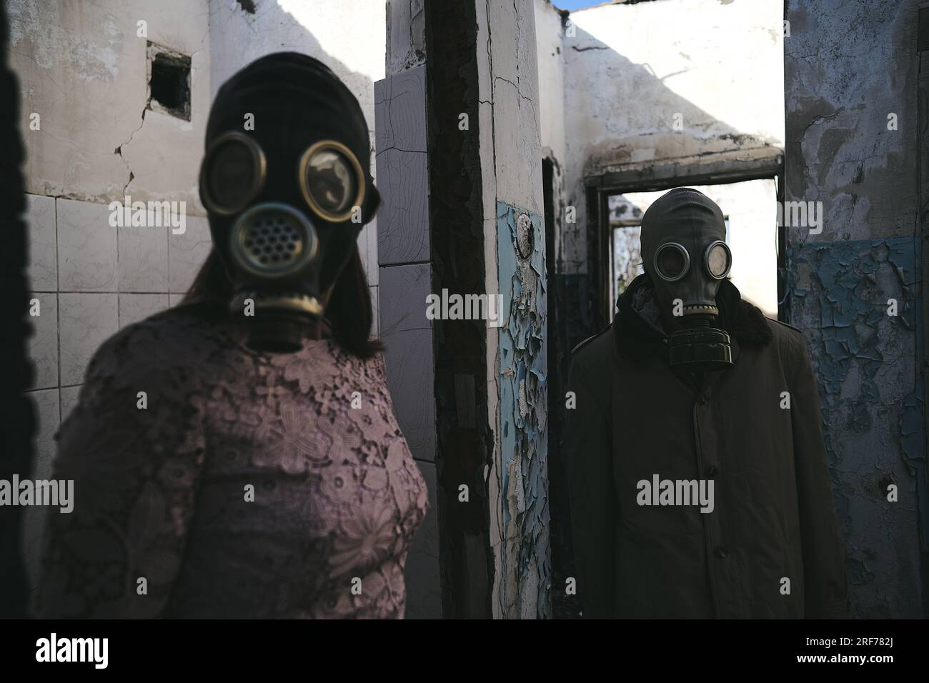 the woman in a gas mask staying in front of a man in destroyed building ...