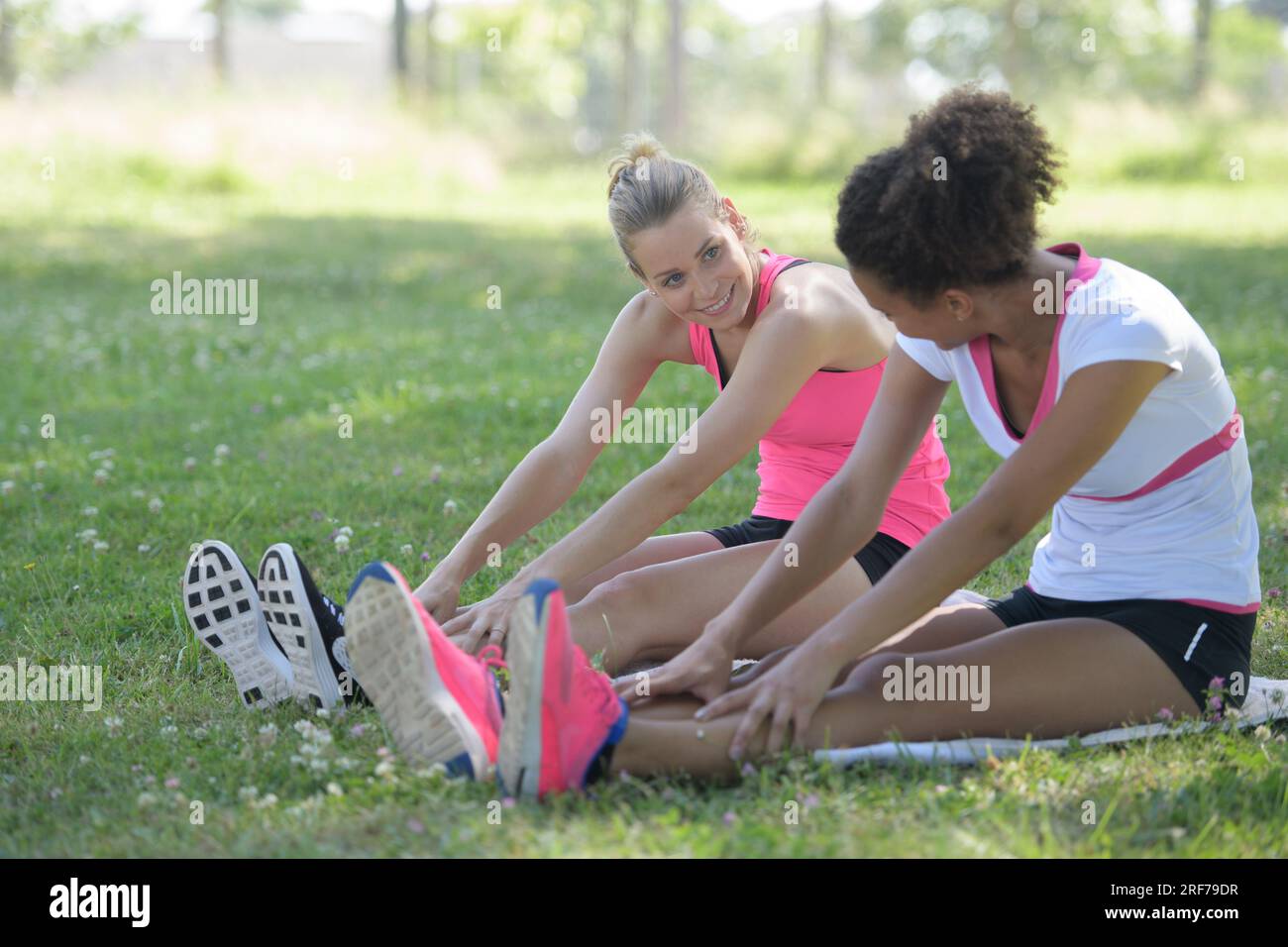 women sat on grass stretching forward towards their feet Stock Photo ...