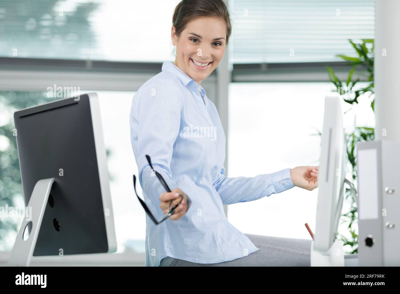 secretary sitting on office table holding her glasses Stock Photo - Alamy