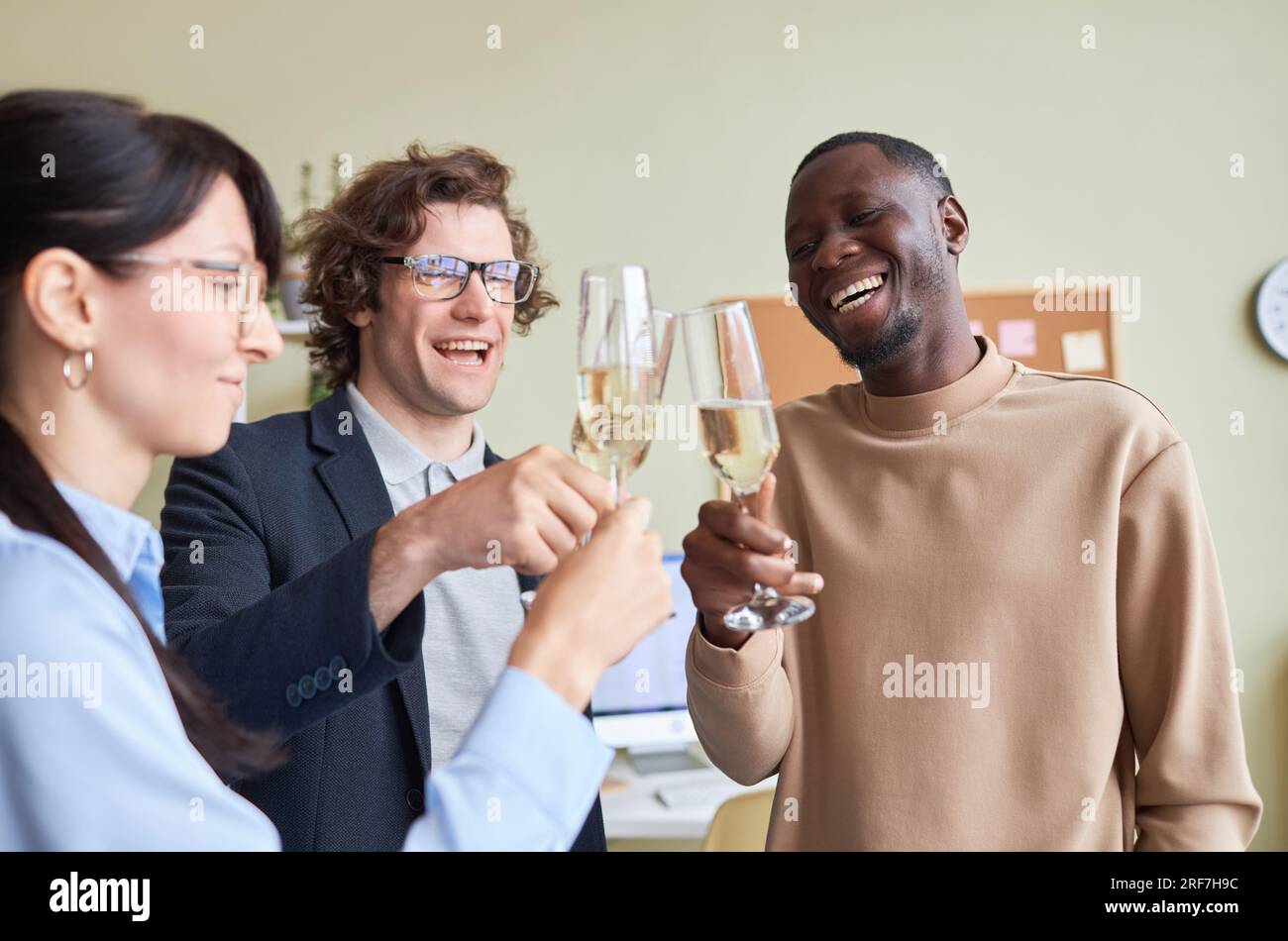 Portrait of three colleagues clinking champagne glasses in office and ...