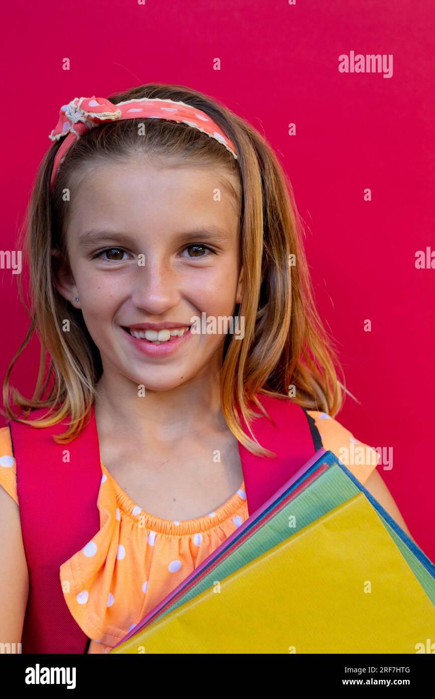 Happy caucasian schoolgirl with school bag and books over pink ...