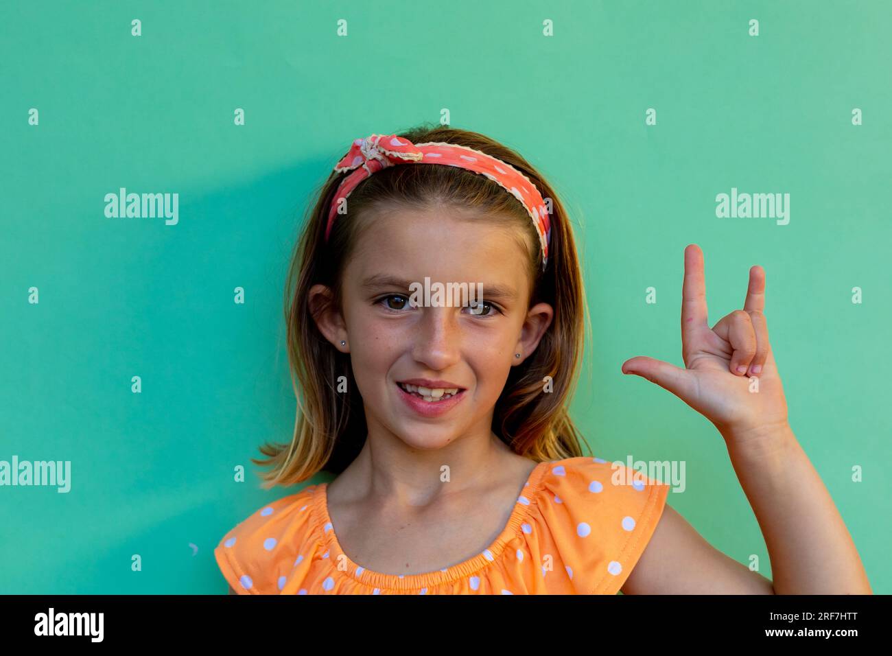 Caucasian schoolgirl doing sign language gesture over blue background ...
