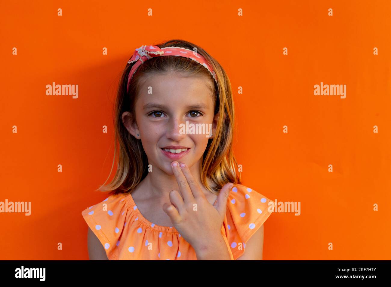 Caucasian schoolgirl doing sign language gesture over orange background ...