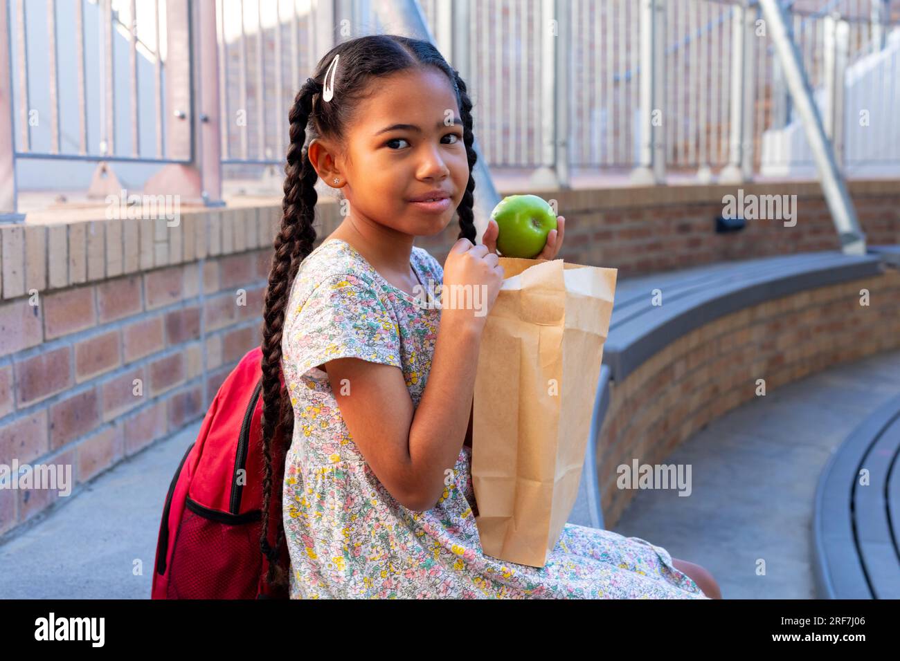 Happy biracial schoolgirl on bench and having healthy lunch eating ...