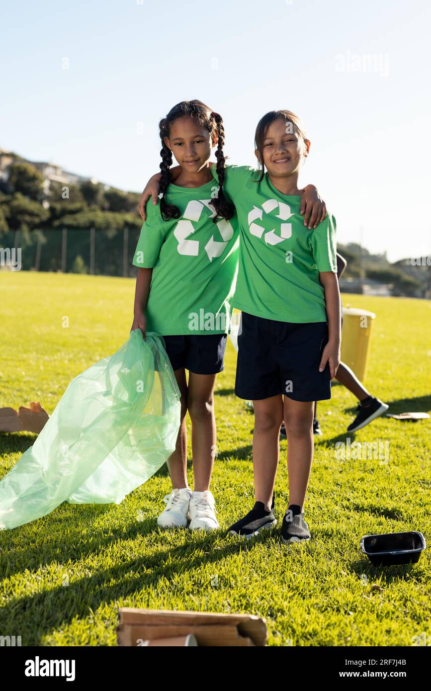 Portrait of happy biracial girls collecting recycling embracing in ...