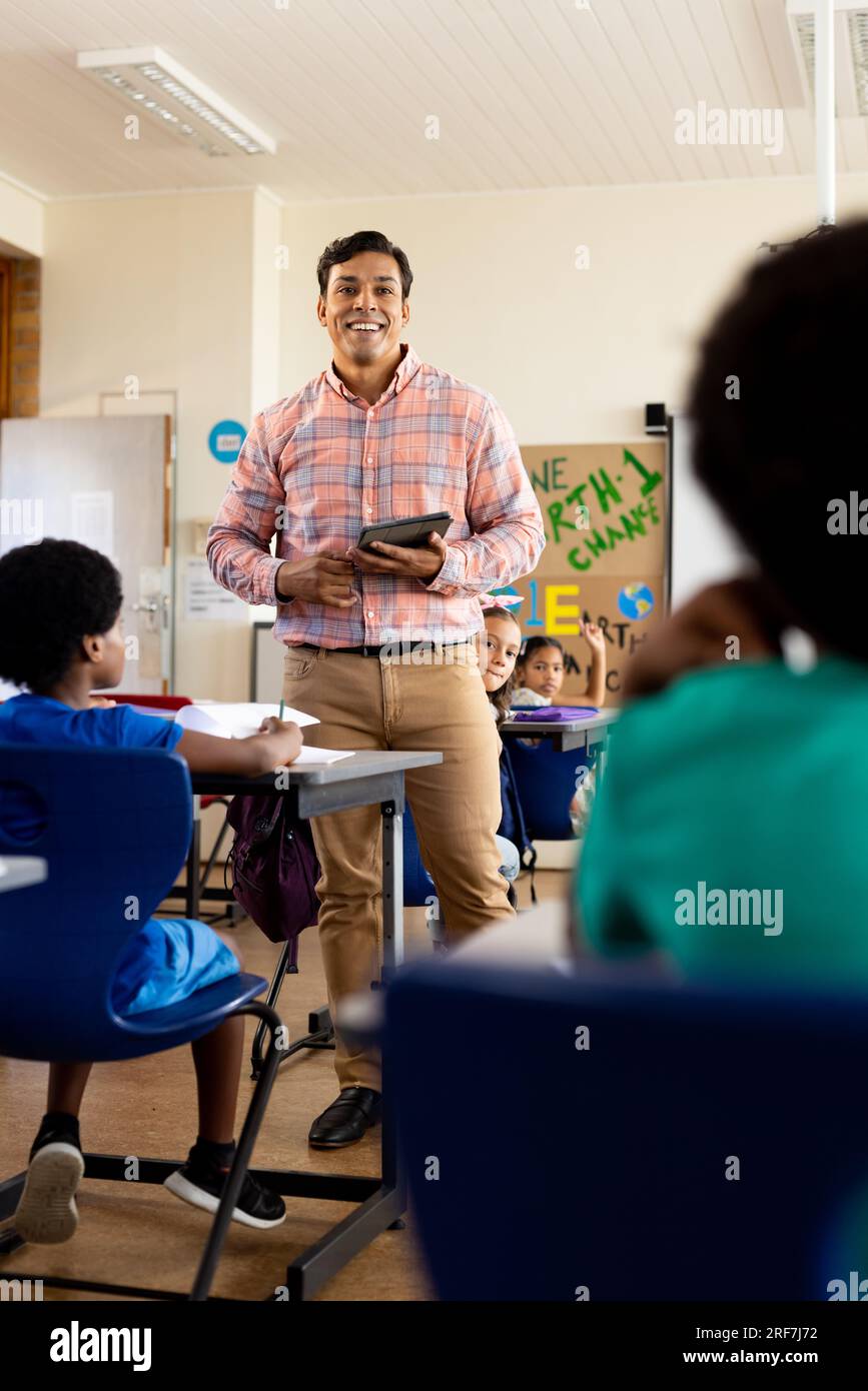 Diverse male teacher with tablet and elementary schoolchildren in class ...