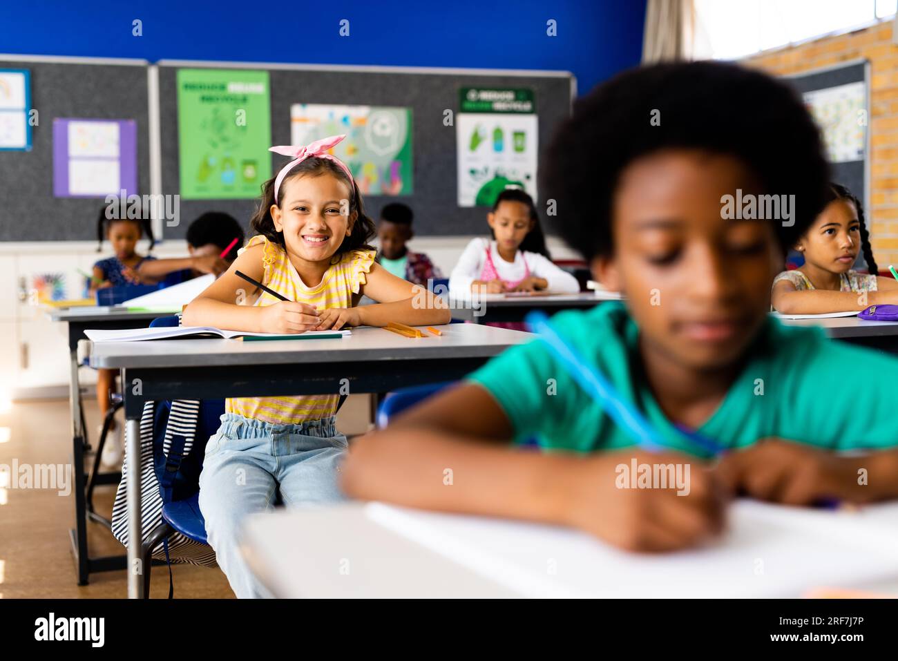Portrait of biracial girl writing at desk with diverse elementary ...