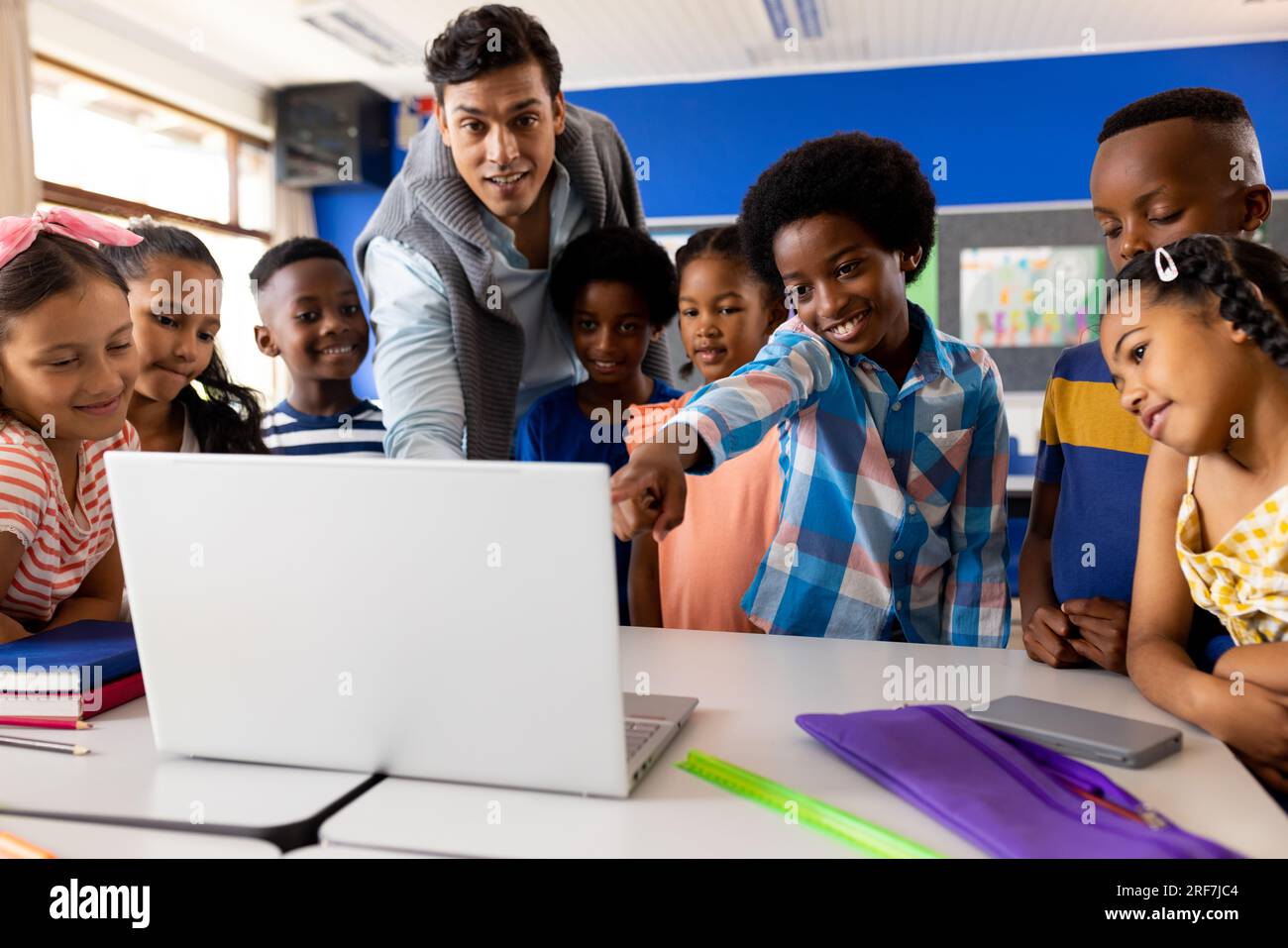 Diverse male teacher using laptop teaching children in elementary ...