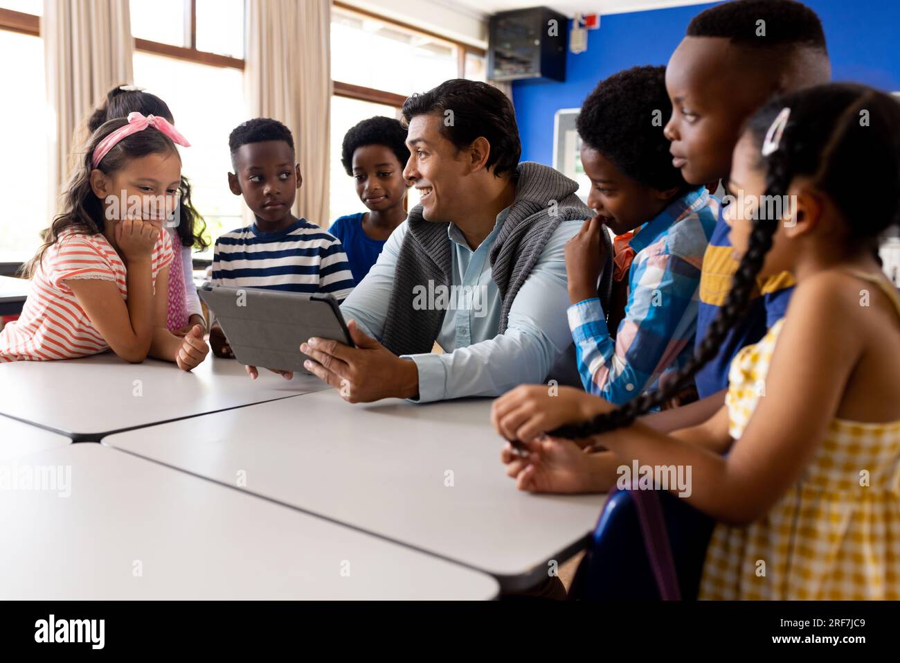 Diverse male teacher using digital tablet teaching children in class at ...