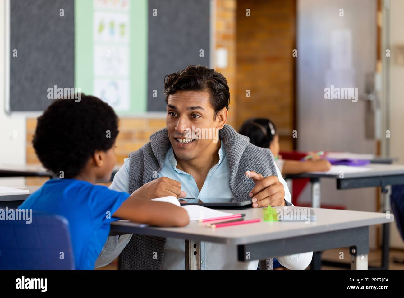 Diverse male teacher using tablet teaching children at desks in ...