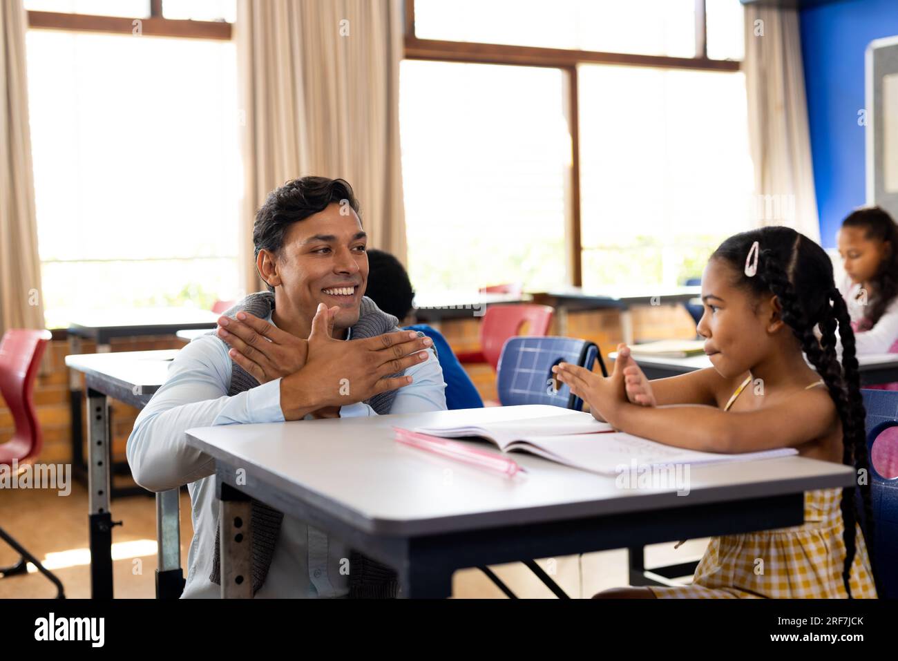 Diverse male teacher teaching school girl using sign language in class ...