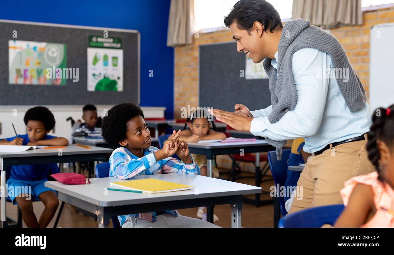 Diverse male teacher teaching school boy using sign language in class ...