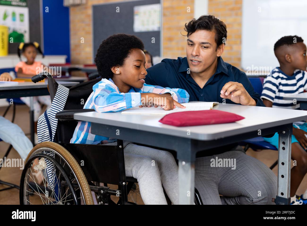 Biracial male teacher helping schoolboy sitting in wheelchair in ...