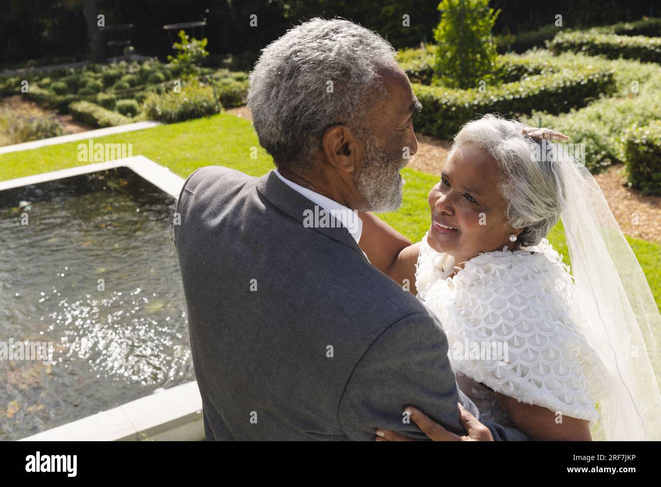 Happy senior biracial bride and groom dancing in garden at sunny ...