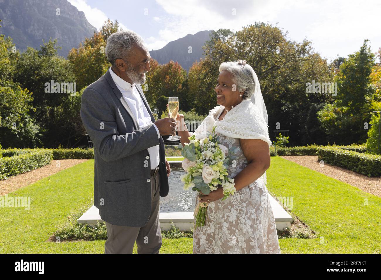 Happy senior biracial bride and groom drinking champagne toast in ...