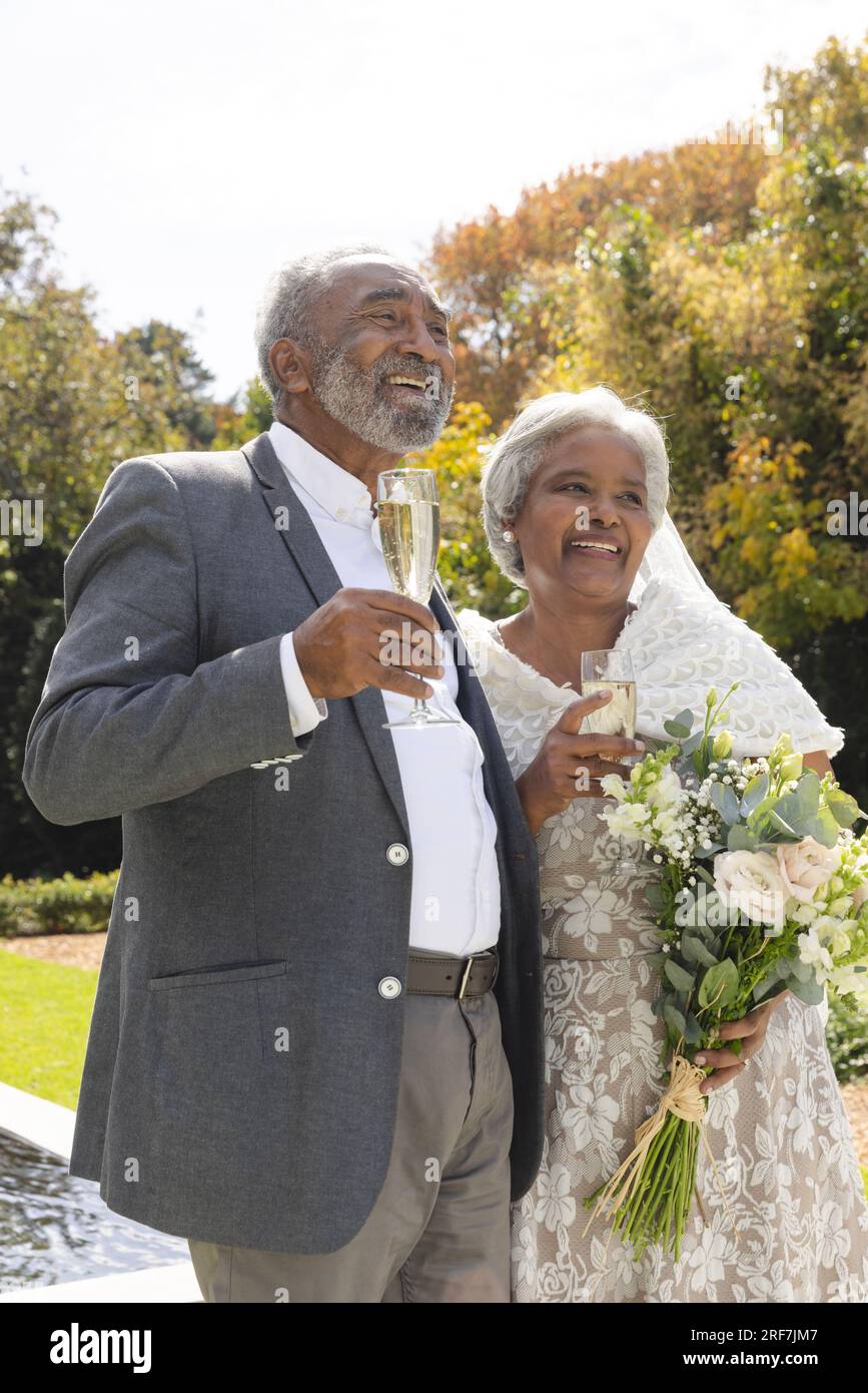 Happy senior biracial bride and groom drinking champagne toast in ...