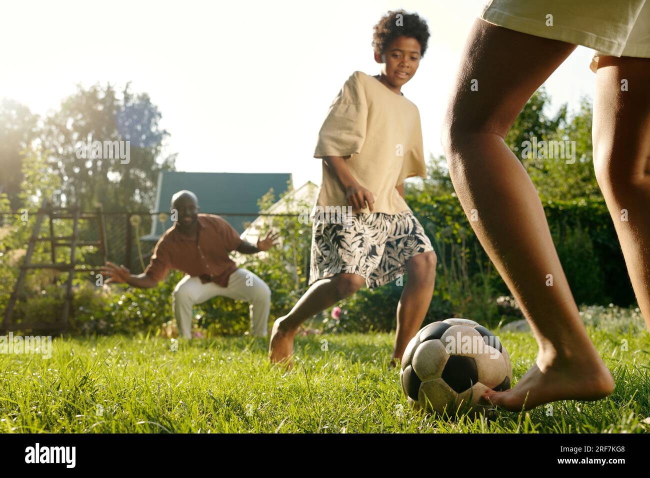 Legs of barefoot girl kicking soccer ball to her brother while playing ...