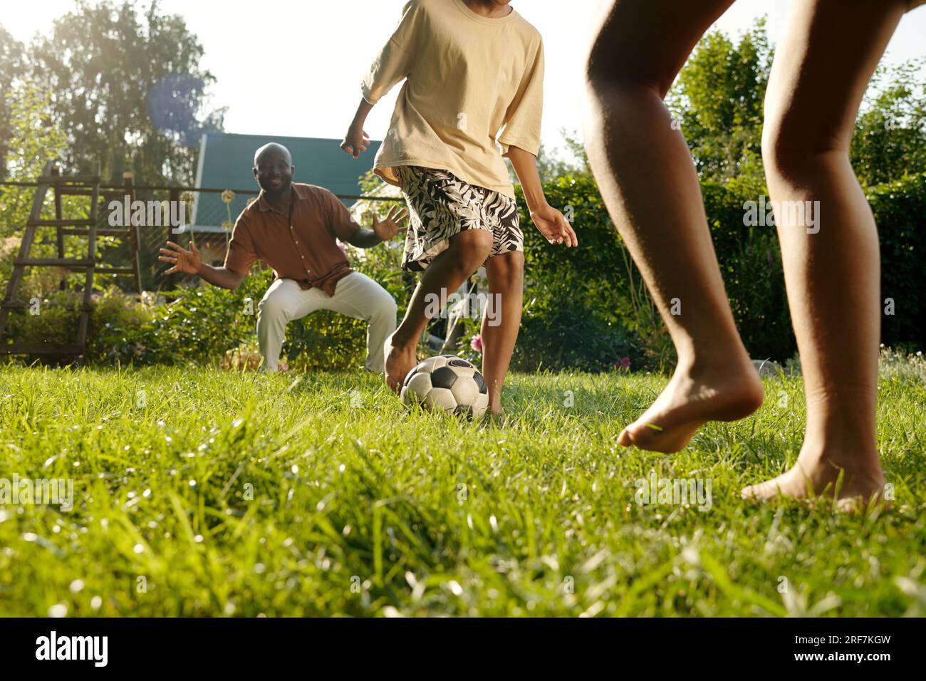 Barefoot children and their father playing footbal on green lawn ...
