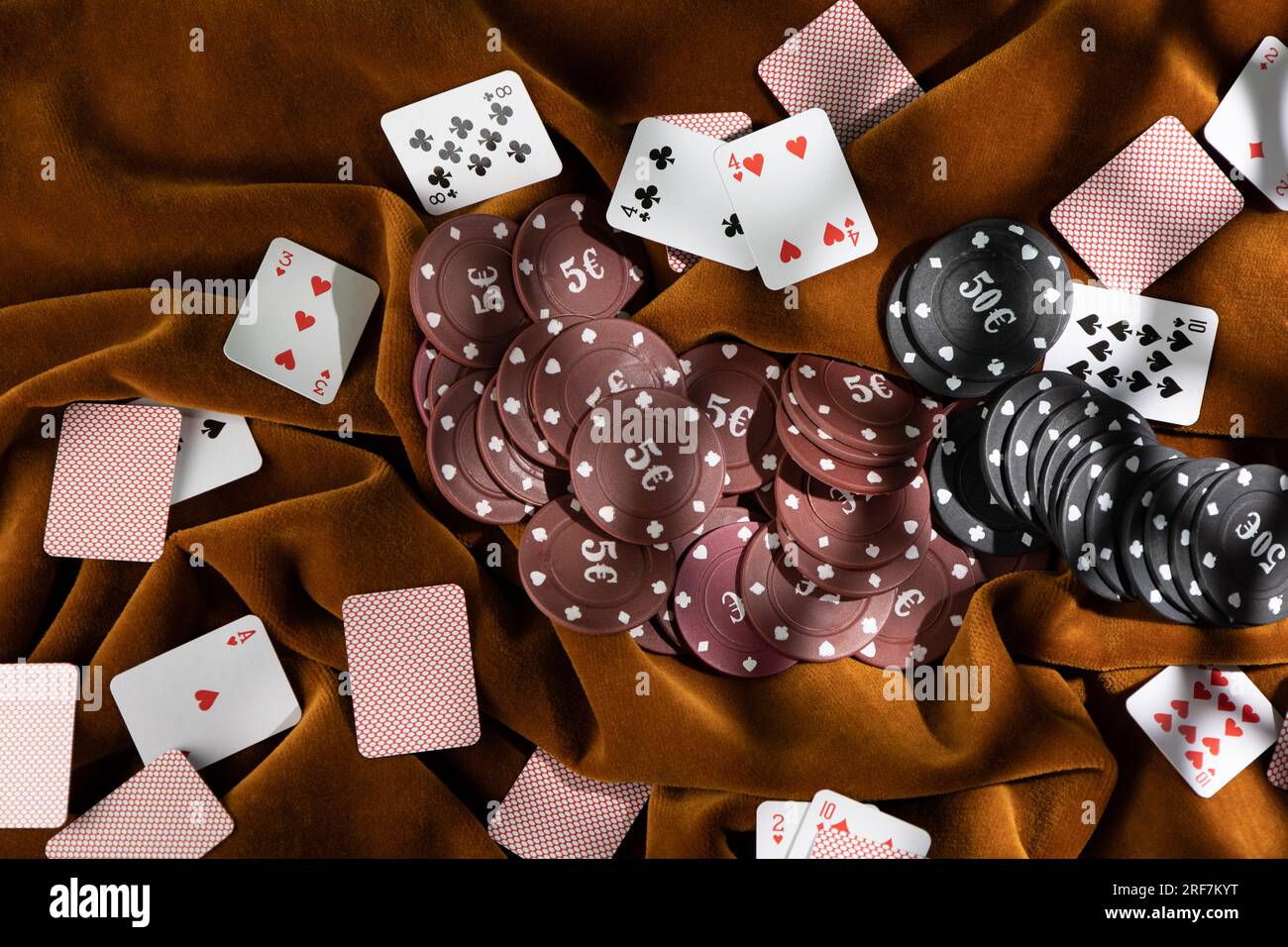 Red and black poker chips are scattered on the brown fabric, and small ...