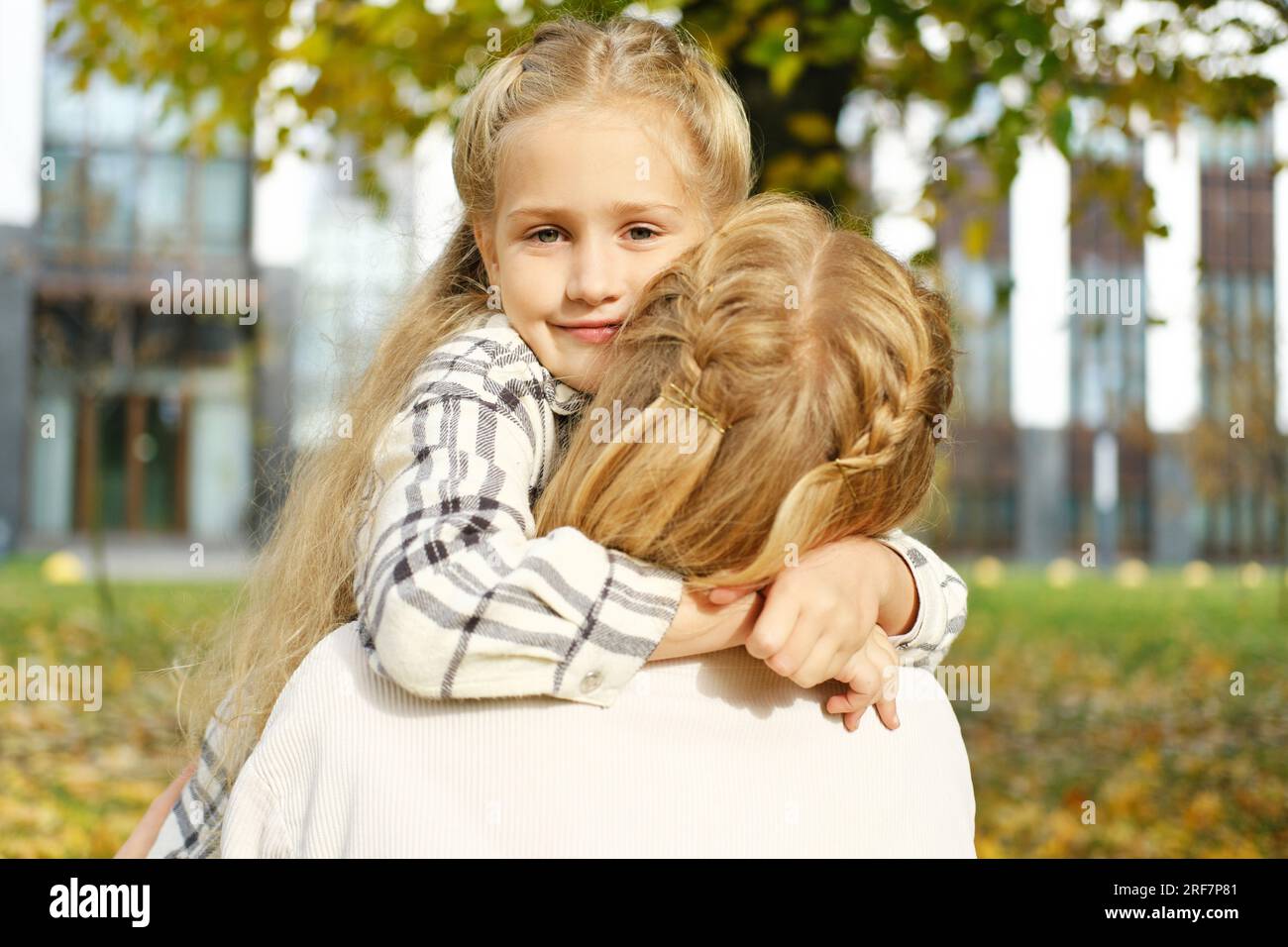 The family spends time together in the autumn park. Daughter hugging her mother's neck, smiling ...