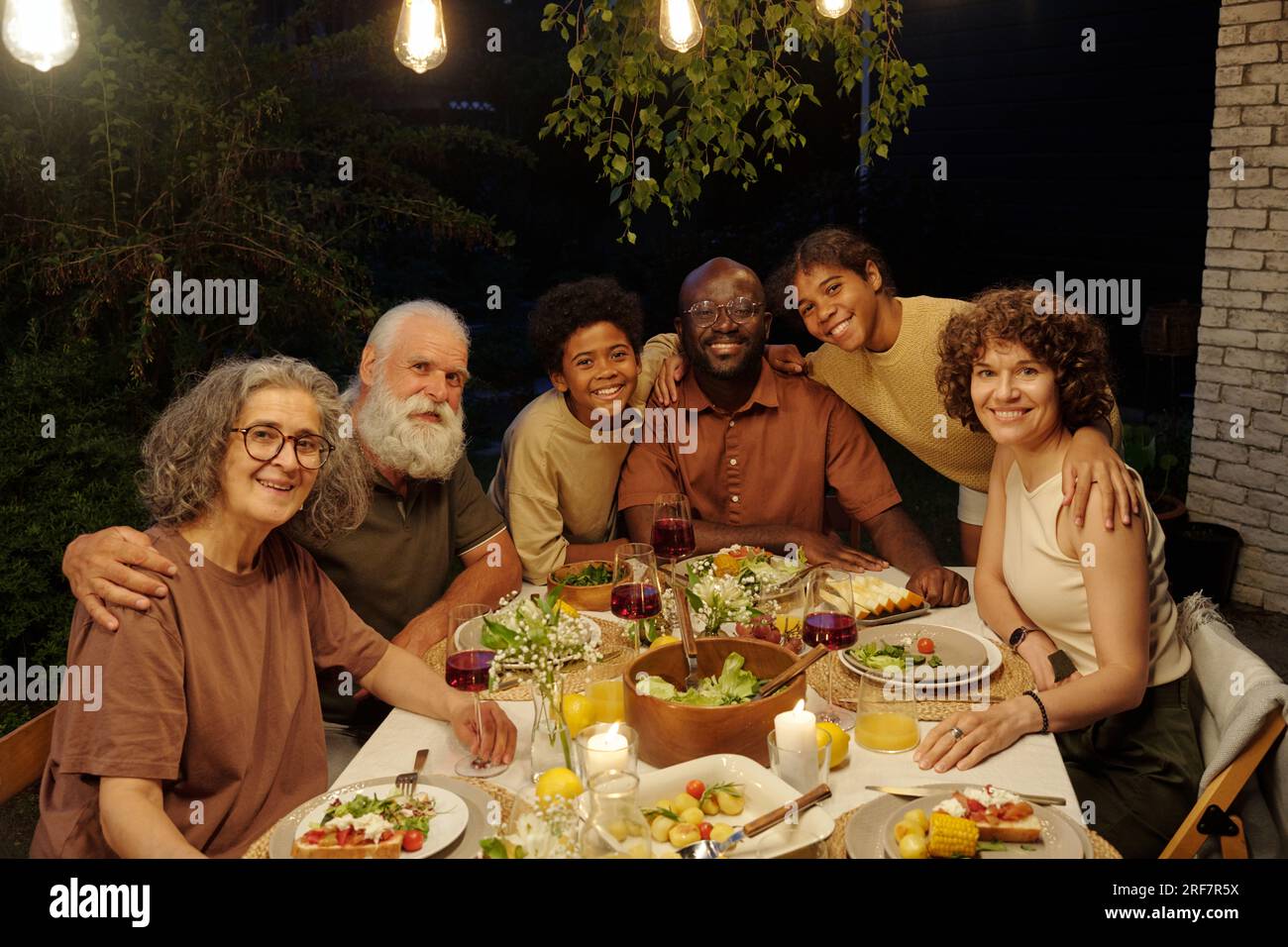 Cheerful intercultural family of three generations sitting by served ...