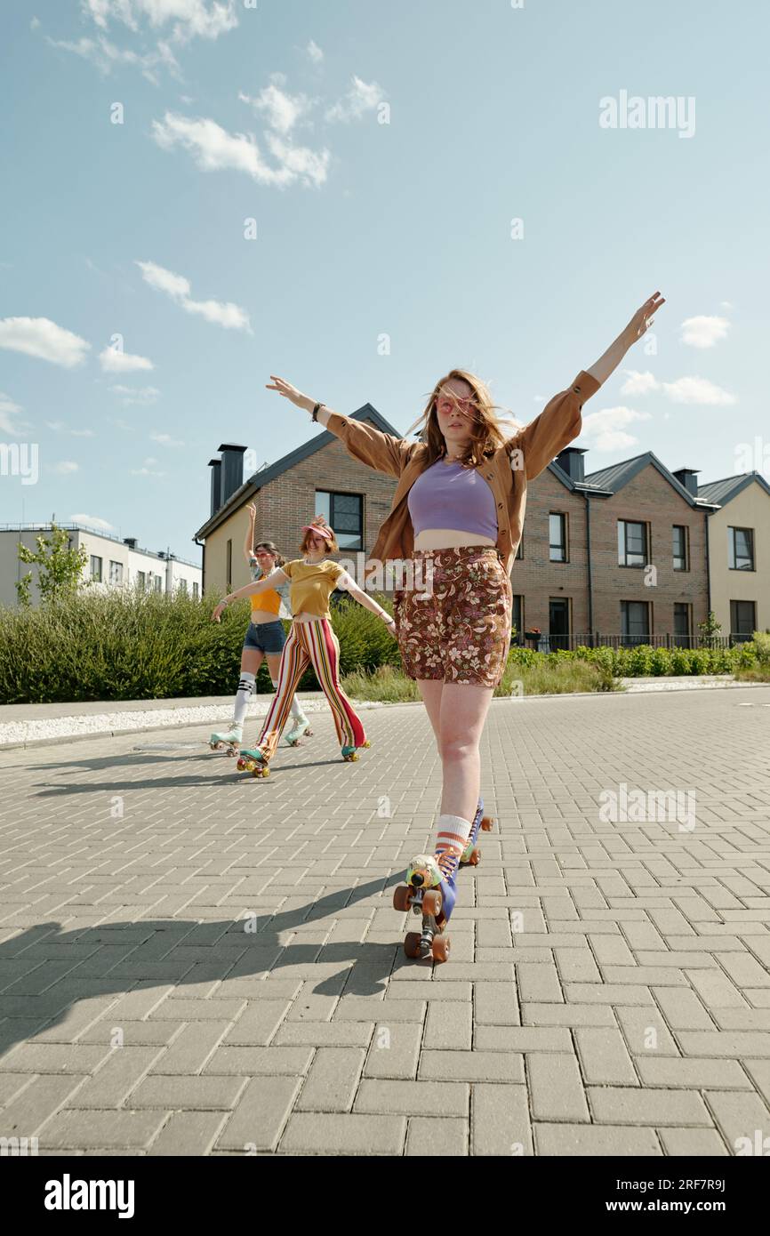 Cute female zoomer in casualwear moving forwards on roller skates along ...