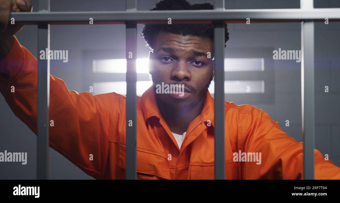 African American man in orange uniform looks at camera and kneads neck ...