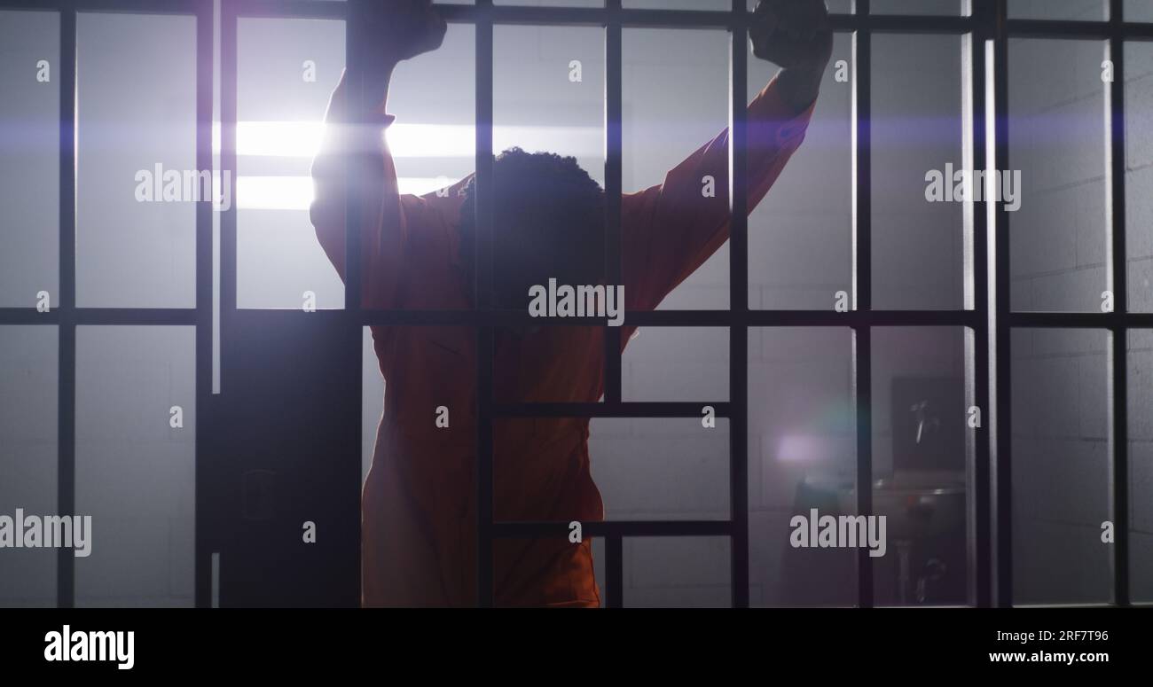 African American prisoner in orange uniform stands up from jail bed and ...