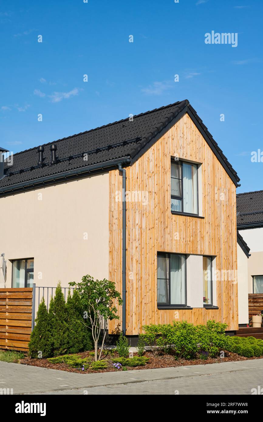 Facade of small two storey cottage with green bushes growing in front ...