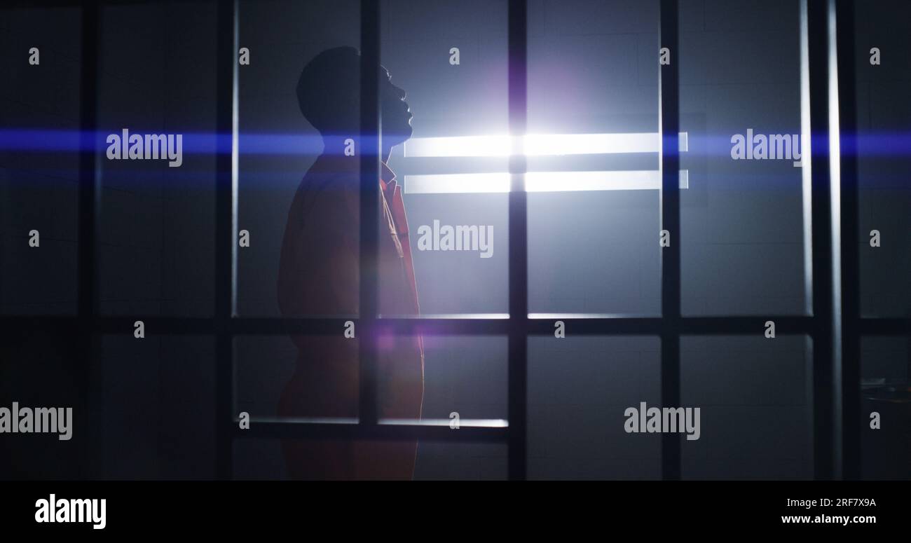 Depressed African American man in orange uniform stands from jail bed ...